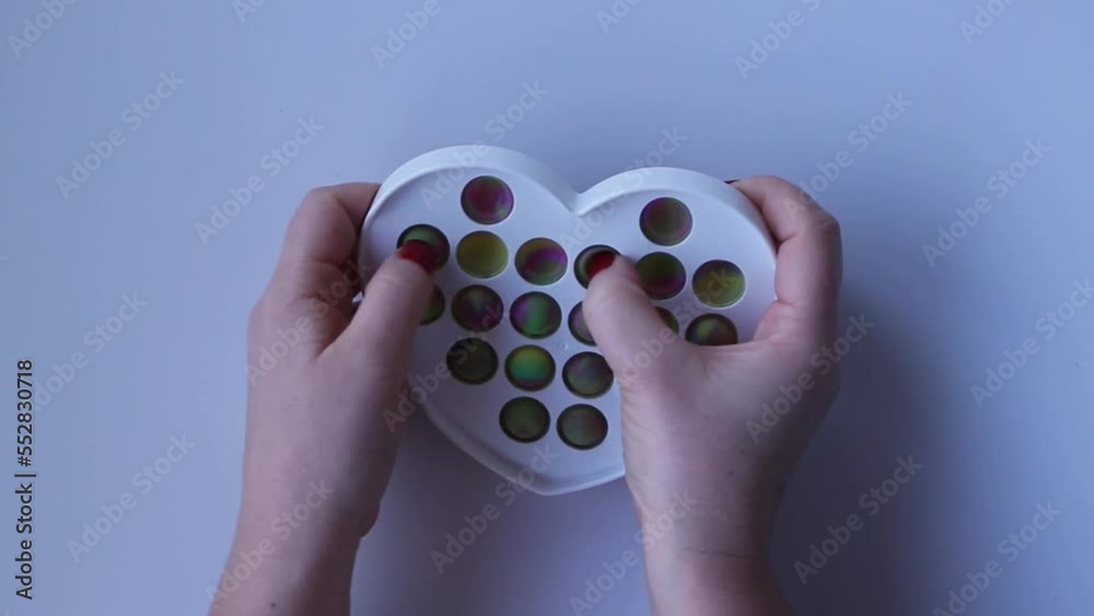 Women hands crumple and play with large heart Pop It close-up top view ...