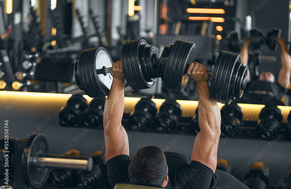 Bodybuilder workout. Muscular strong arms of an athlete lift dumbbells ...