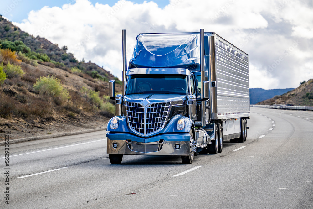 Stylish blue big rig semi truck with chrome parts transporting cargo in ...