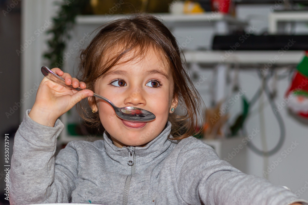 Little girl with brown hair and gray sweatshirt eating and looking at ...