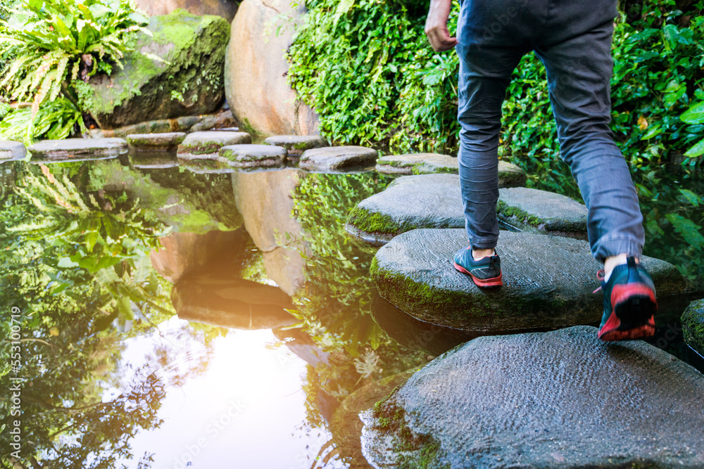 Young man walking crossing a river on stones Stock Photo | Adobe Stock