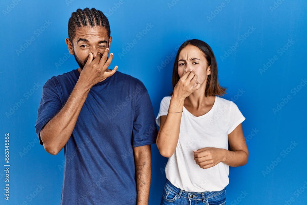 Young hispanic couple standing together smelling something stinky and ...