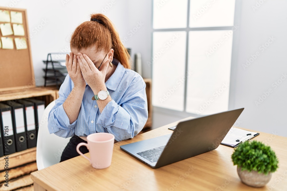 Young redhead woman working at the office using computer laptop with ...