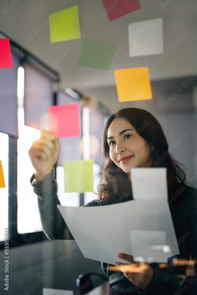 Young smiley attractive,businesswoman using post it notes in glass wall ...