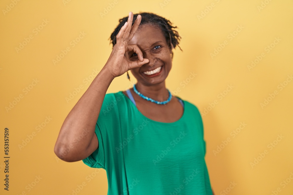 African woman with dreadlocks standing over yellow background doing ok ...