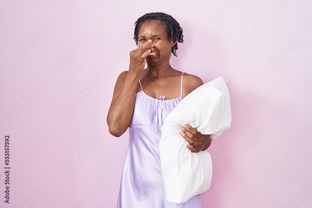African woman with dreadlocks wearing pajama hugging pillow smelling something stinky and ...