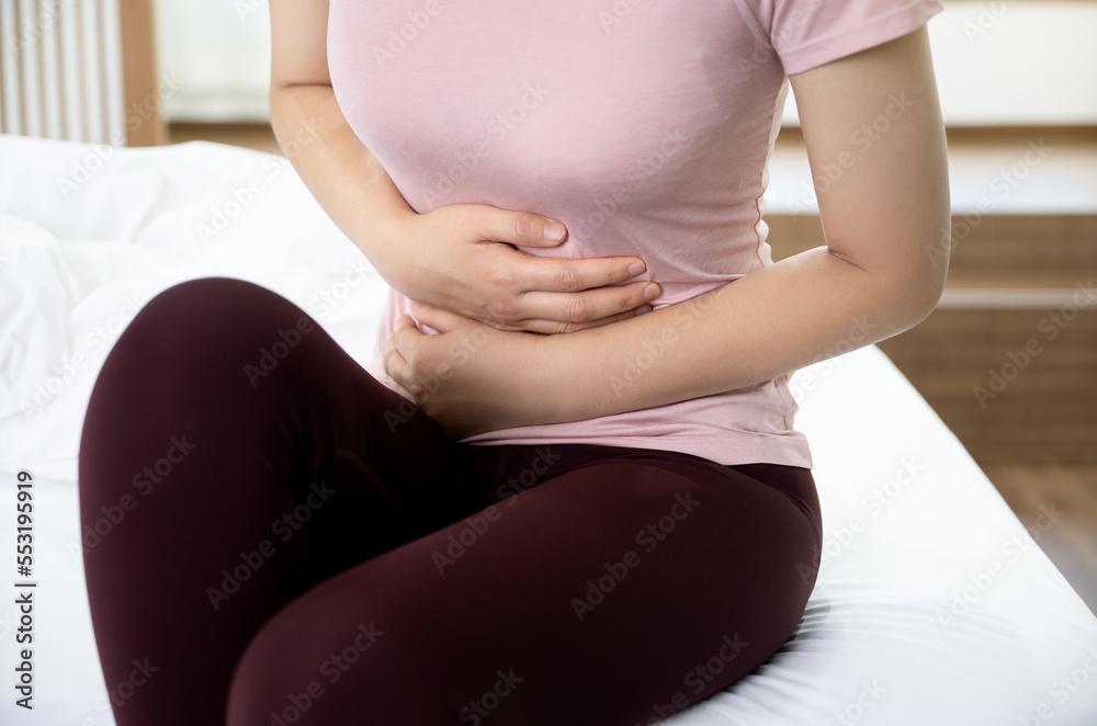 Woman suffering from stomachache is sitting on the bed and clutching ...