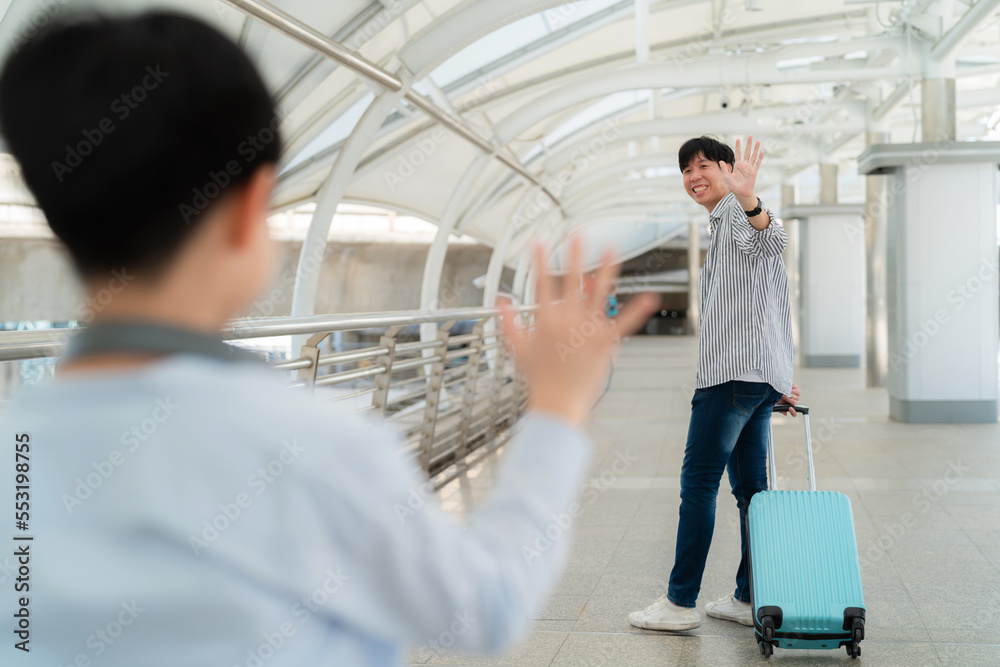Father dragging a suitcase and raise his hand bye to his son with smile ...