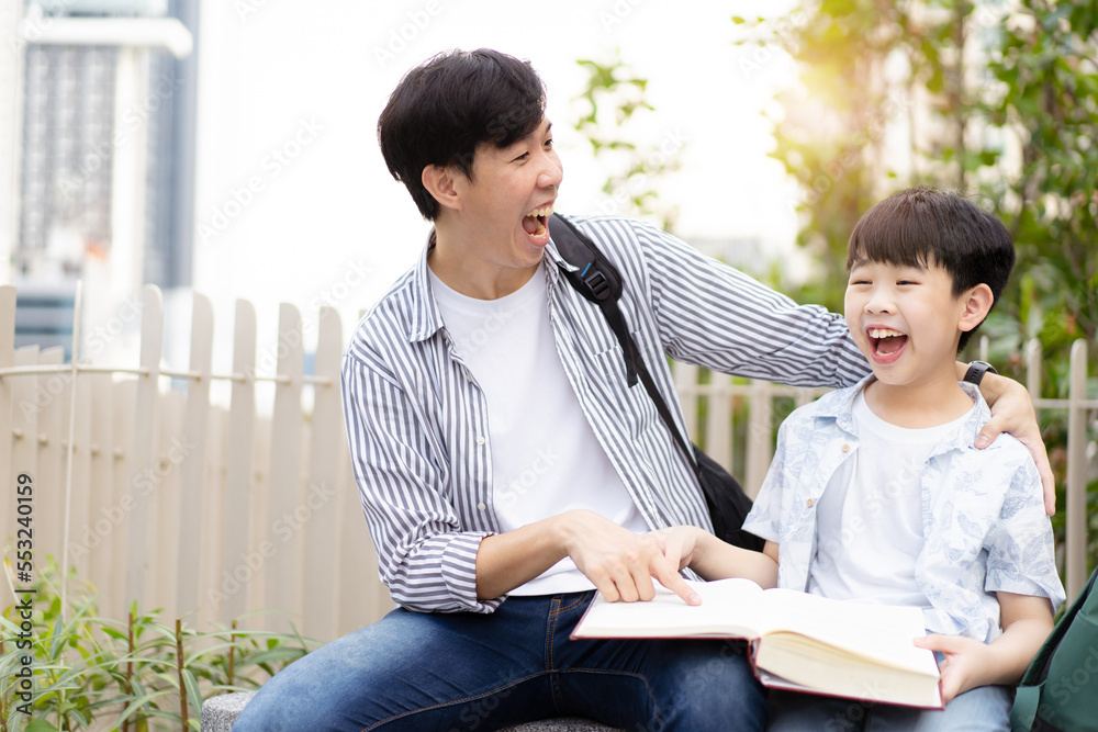 Cheerful happy Asian little boy and his father reading a book or fairy ...