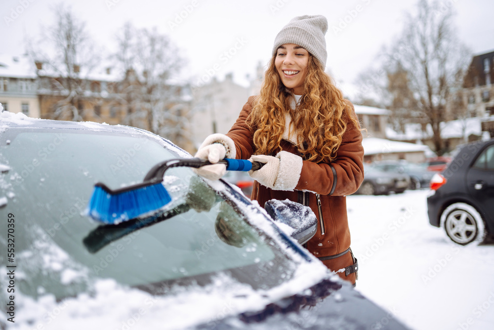 Portrait of young woman cleaning snow off car during winter snowfall ...