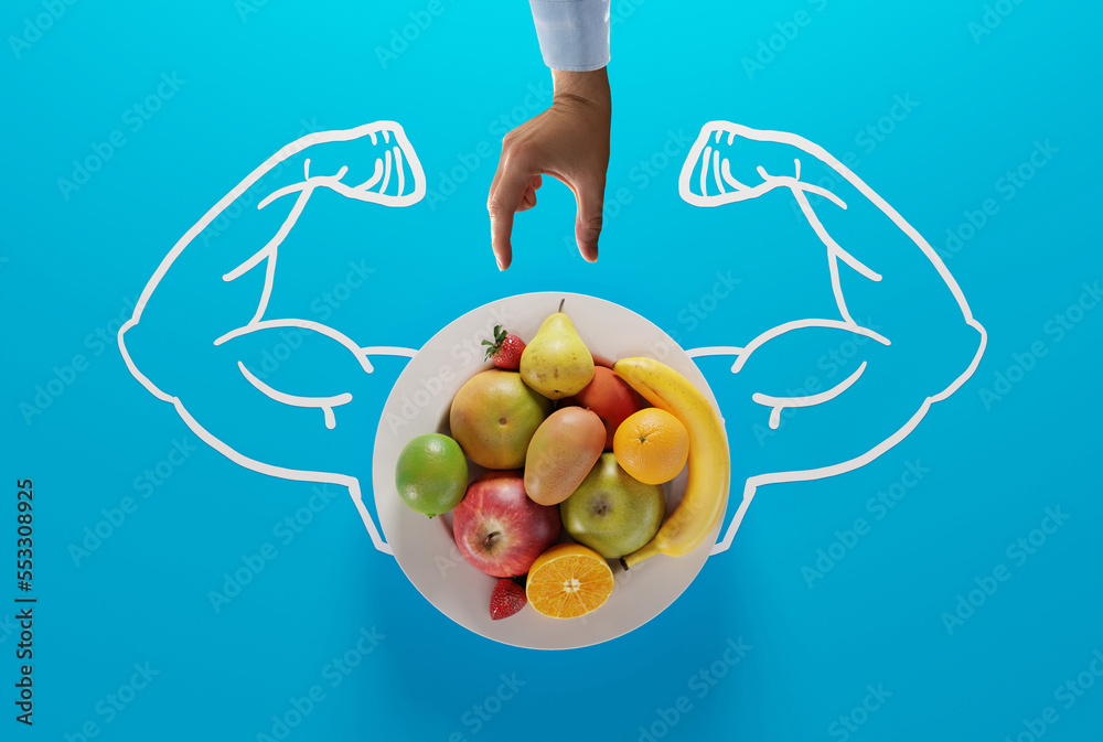 Muscles on the background of a plate and hand try to reach fruits. The ...