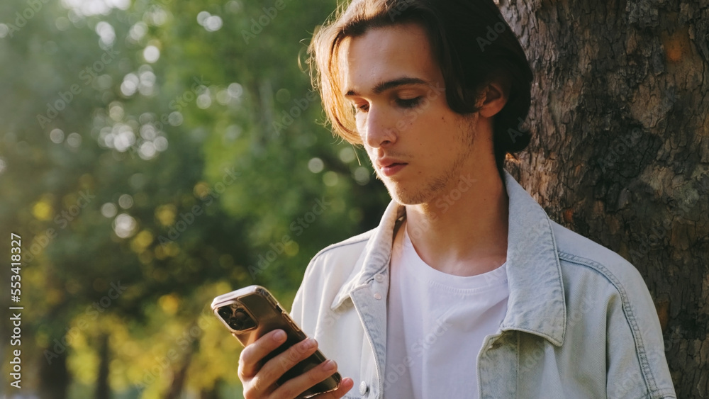Sad man with a mobile phone in the park. Young guy received an sms with ...