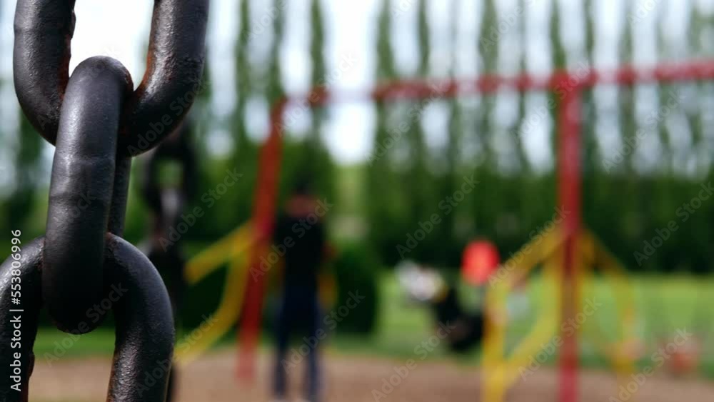 Park swing metal chain with family playing in the background defocussed ...