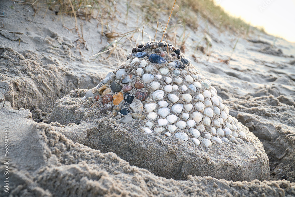 Sand castle with shells and sand. Moat around the castle in front of ...
