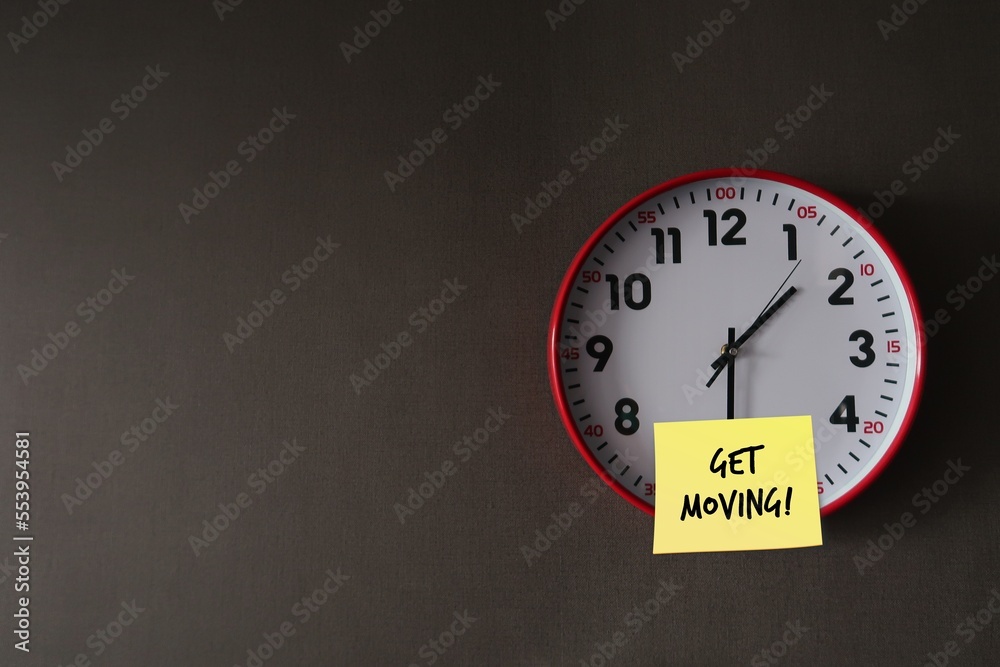 Wall clock on gray office wallpaper with handwritten note GET MOVING ...