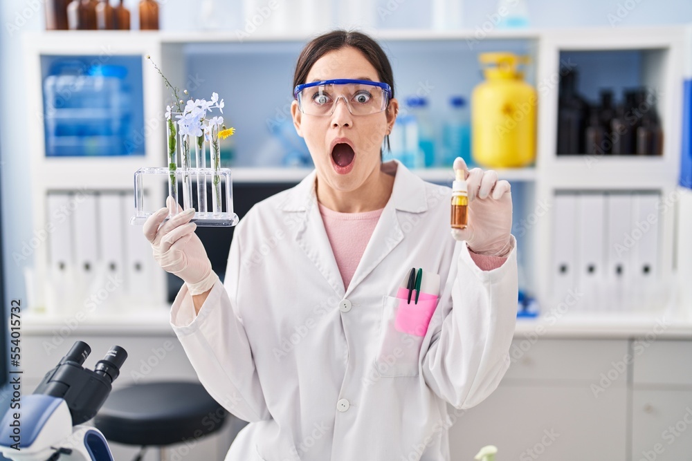 Young brunette woman working at scientist laboratory afraid and shocked ...