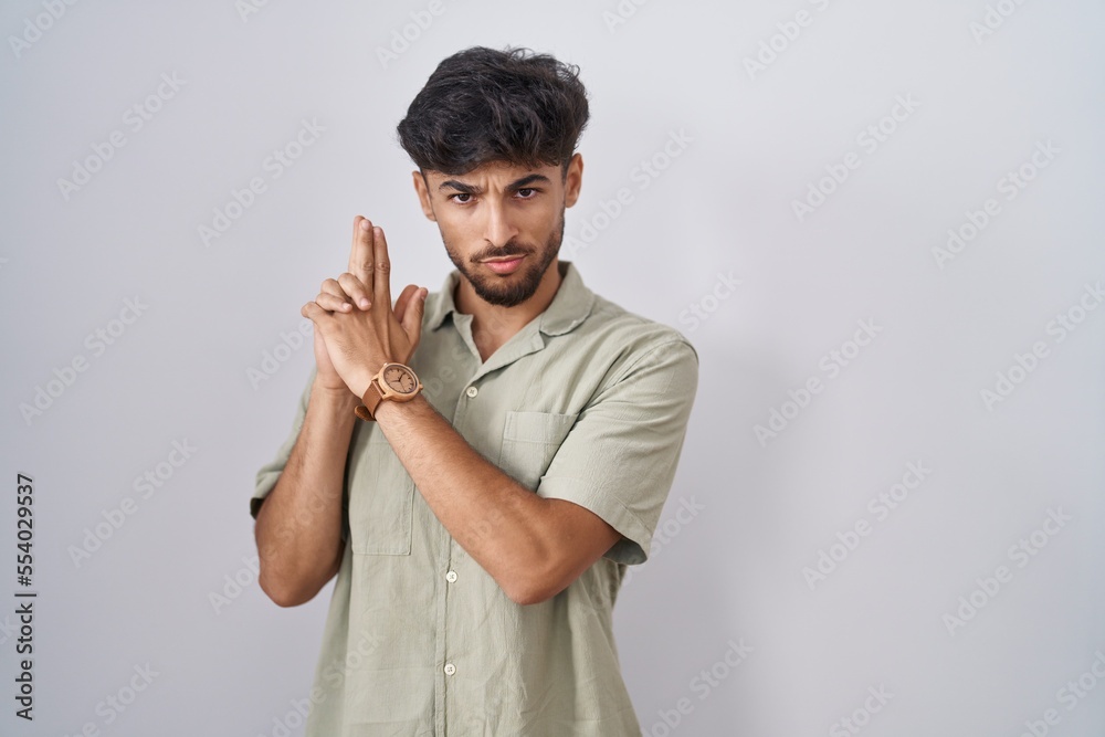 Arab man with beard standing over white background holding symbolic gun ...