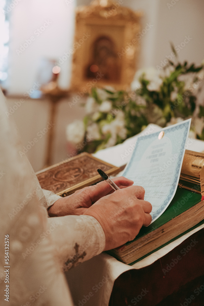 hands of a Christian priest signing a baptismal certificate during a ...