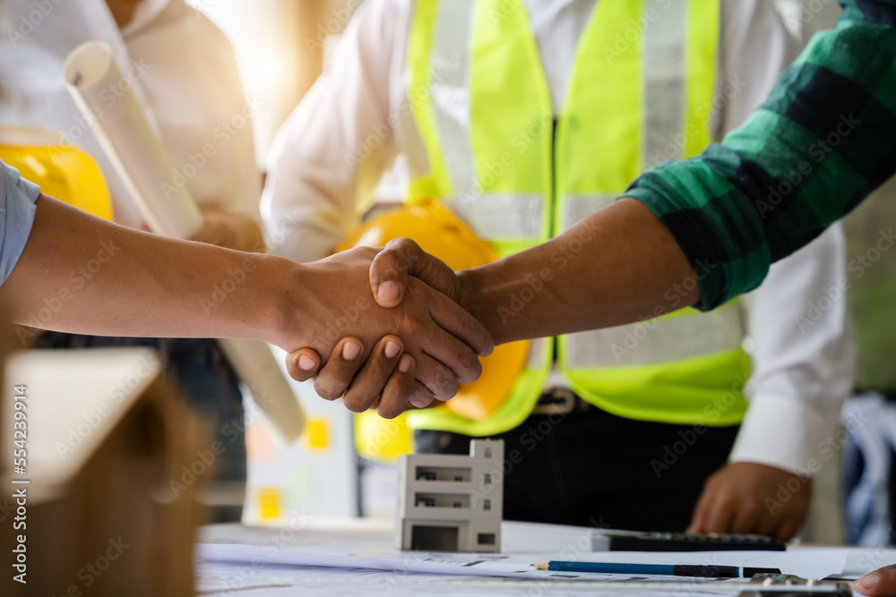 Construction workers, architects and engineers shake hands while ...
