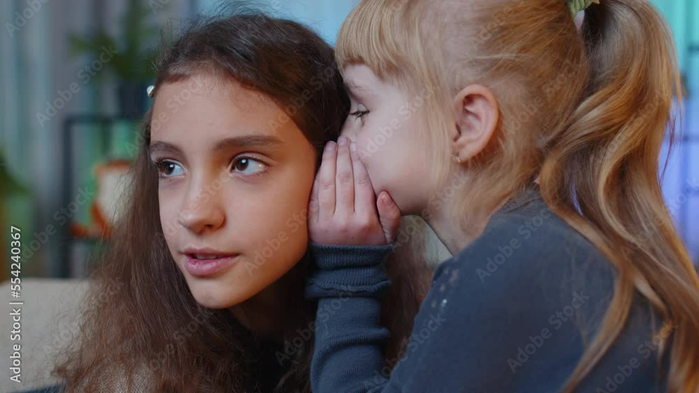 Teenage child whisper news rumors in ear to little sister kid girl ...