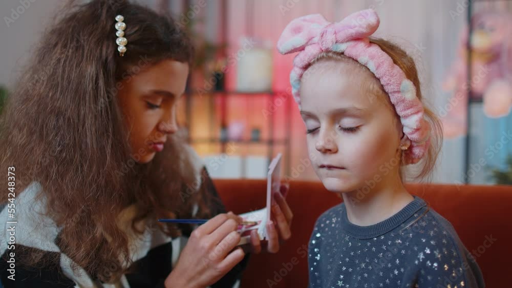 Teenage child helps or teaches to do face makeup her little sister kid ...
