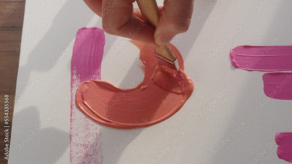 Top down young woman hand paints coral color with wide brush on small ...