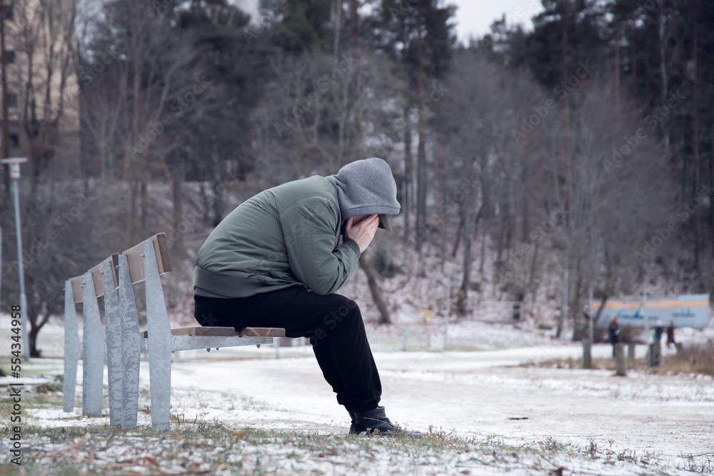 Lonely and sad man sitting on a park bench in snowy winter scenery ...