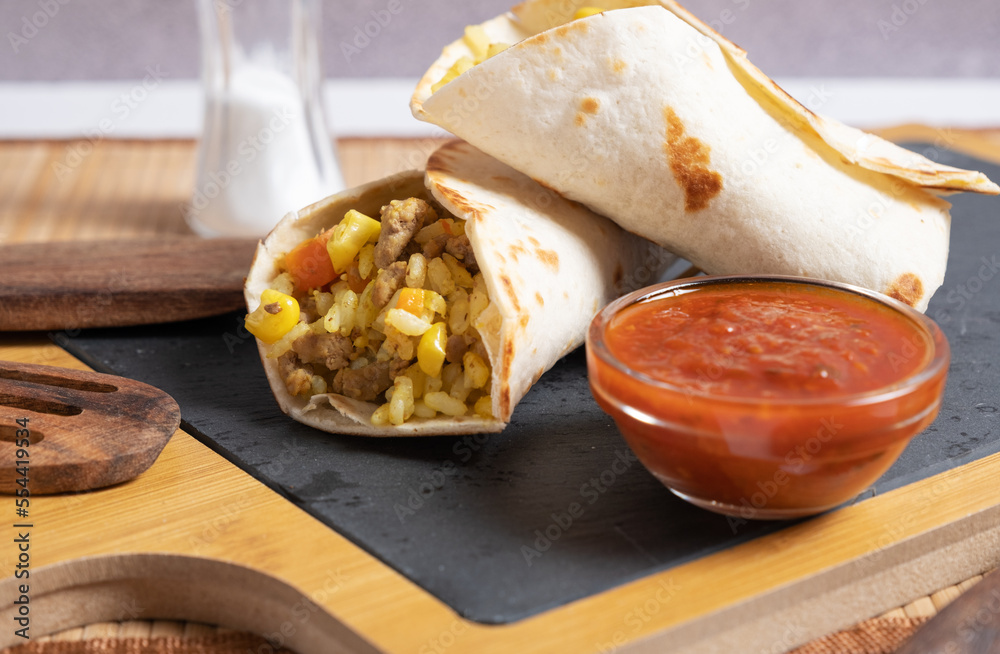 Two close-up burritos filled with rice, meat, corn with spicy tomato ...