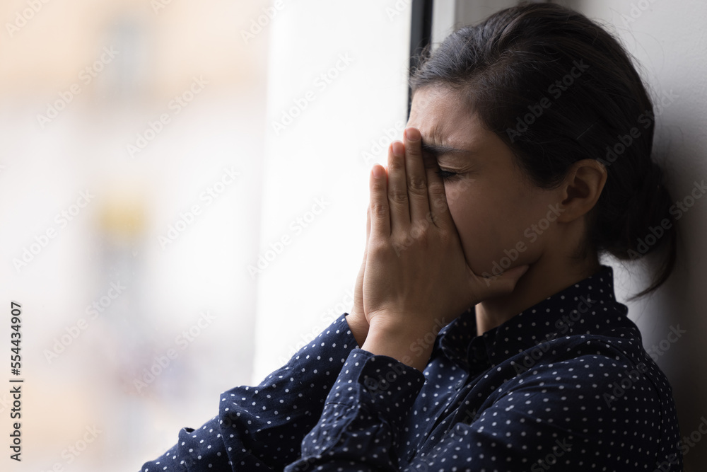 Frustrated unhappy young Indian woman crying at window, covering face ...