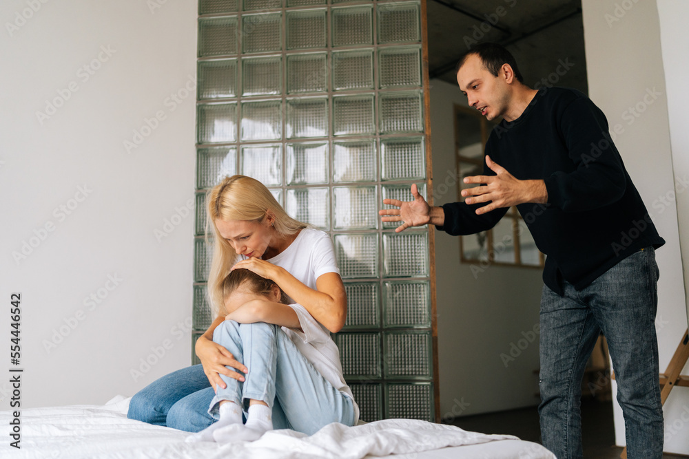 Portrait of scared mother and daughter hugging each other while father ...