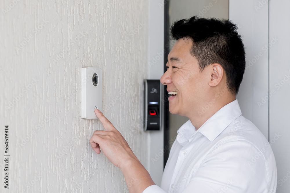 Close-up photo. A young Asian man rings an electronic doorbell on the ...