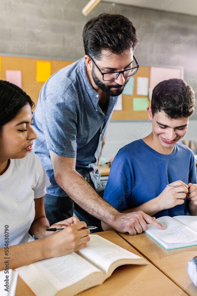Male teacher helping high school students doing exercises in classroom ...