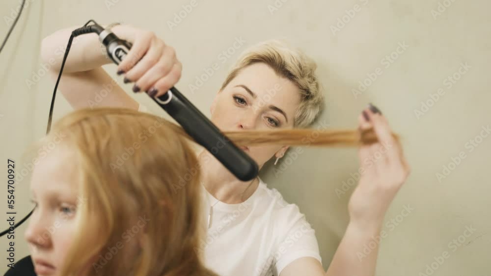Mom does her daughter's hair, curls her hair with a hair straightener ...