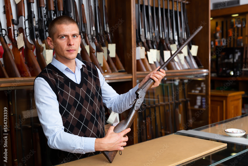 Confident male owner of armory shop standing behind counter and ...