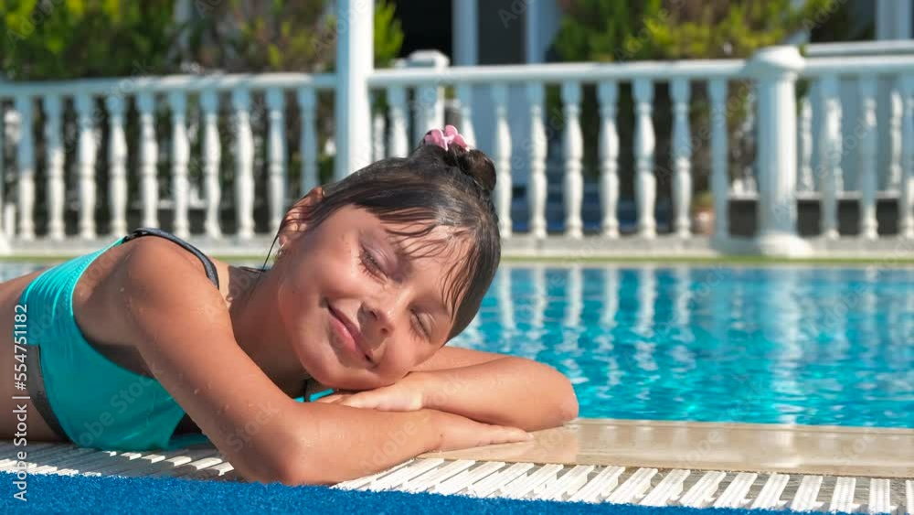 Child sunbathing against pool. A happy little girl sunbathing after ...