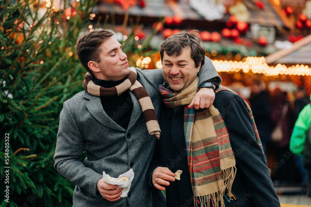 Smiling man eating trdelnik with arm around father enjoying at ...