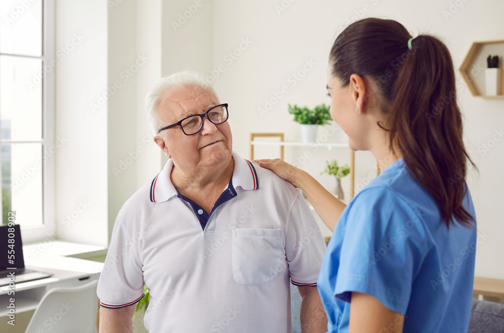 Caring medical nurse comforting senior patient in office. Side view of ...