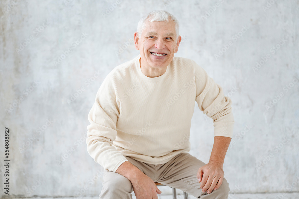 Happy senior man sitting on stool in front of wall at home Stock Photo ...