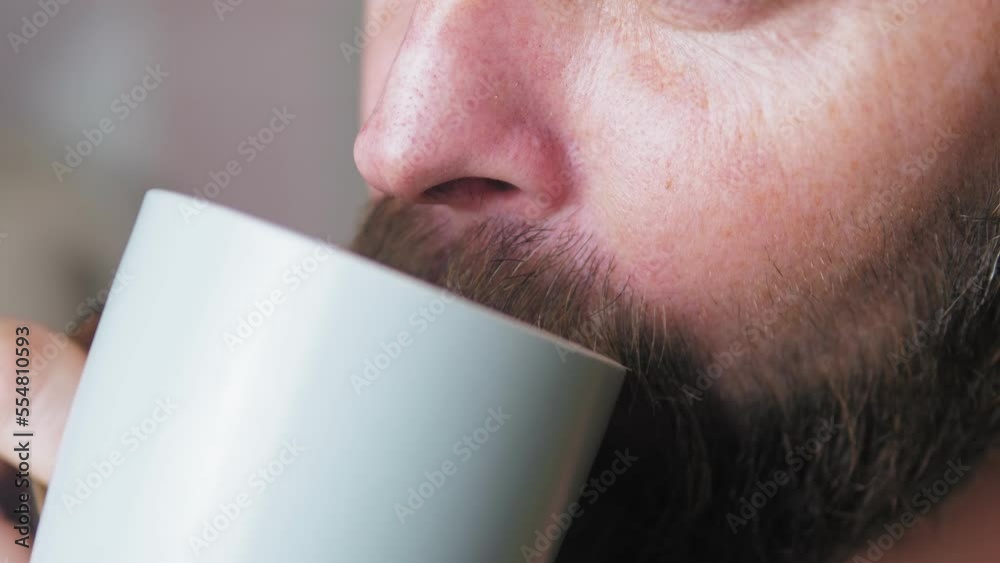 Caucasian bearded man drinking coffee in the kitchen. Close-up of a man ...