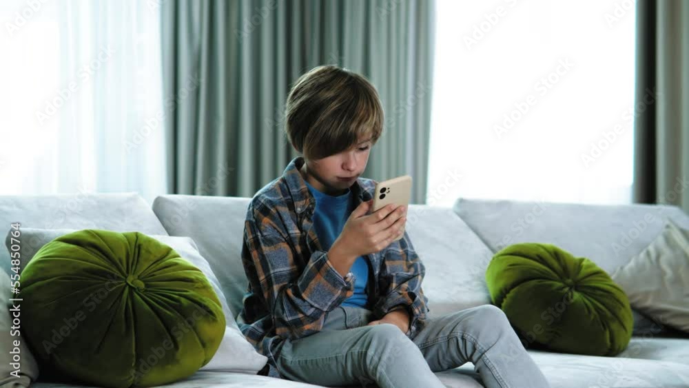 Attractive boy teenager sitting on the sofa in the living room and ...