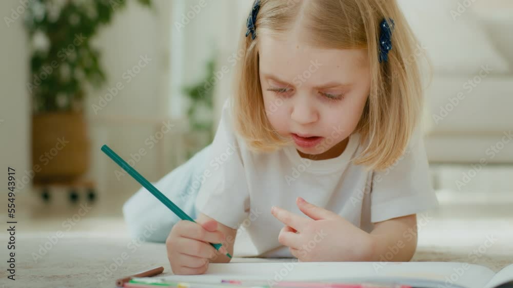 Cute concentrated Caucasian little kid girl draw color pencil lying on ...