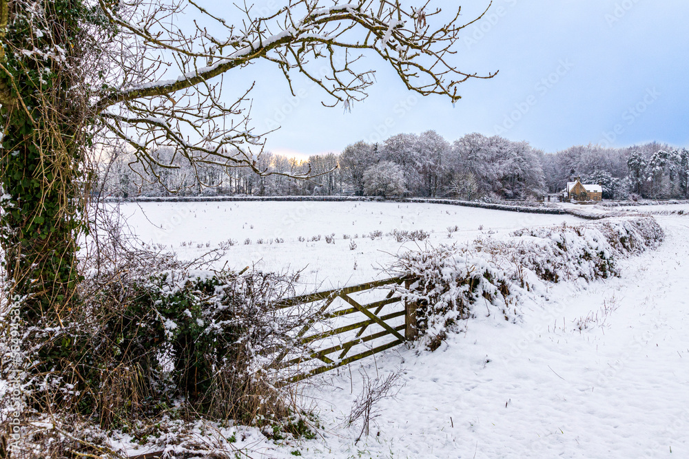 Dusk falling on early winter snow on the lodge and gates to Miserden ...