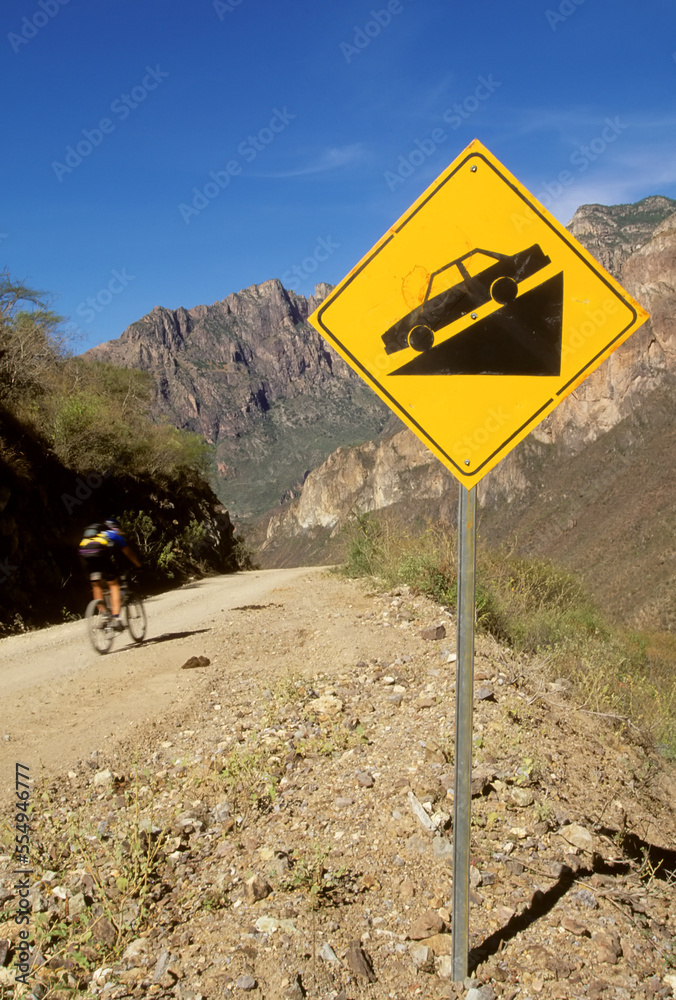 A biker heads downhill past a steep slope sign.; Batopillas Canyon ...