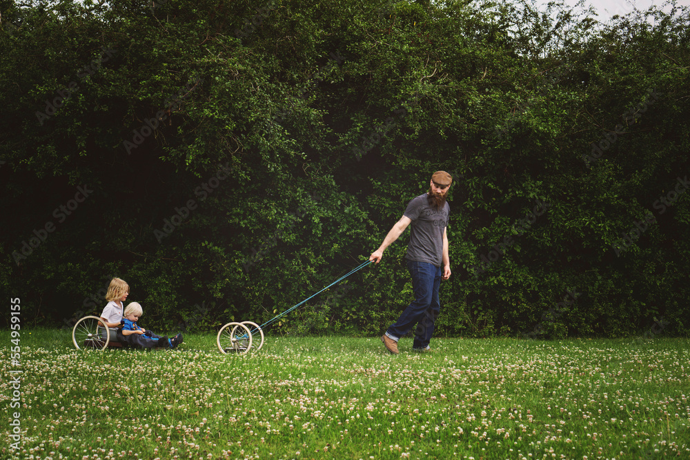 Father pulling his two boys along on a go kart. Stock Photo | Adobe Stock