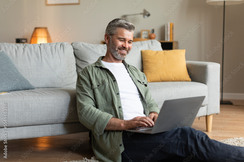 Smiling old caucasian male typing on computer, chatting on social media ...