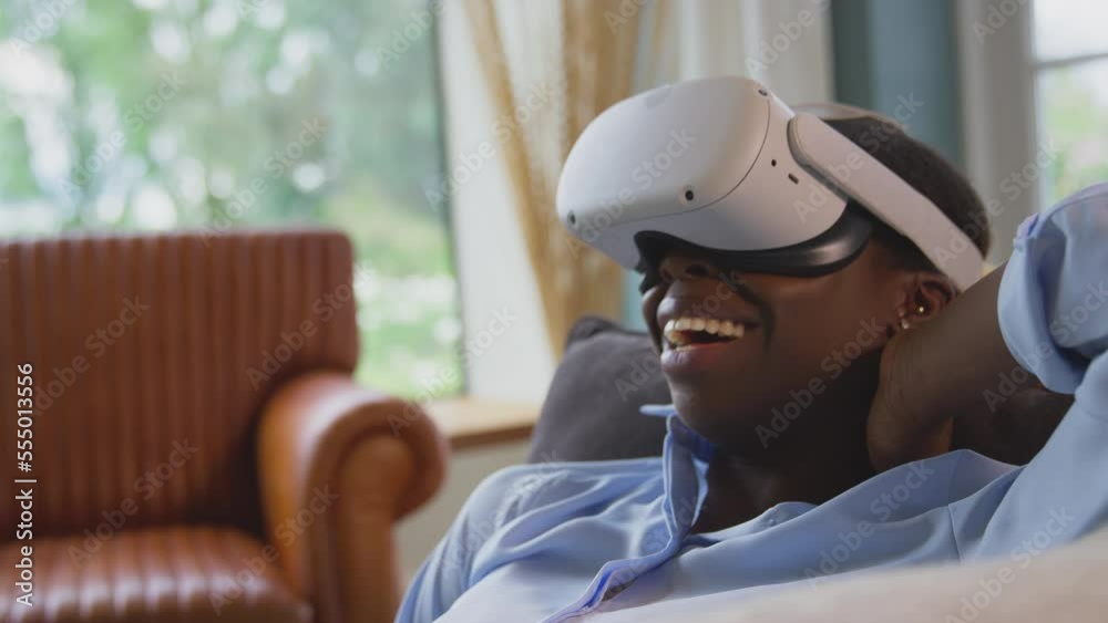 Woman relaxing lying on sofa at home laughing wearing VR headset and ...