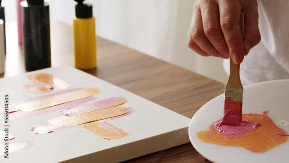 young woman hand paints coral color with wide brush on small white ...
