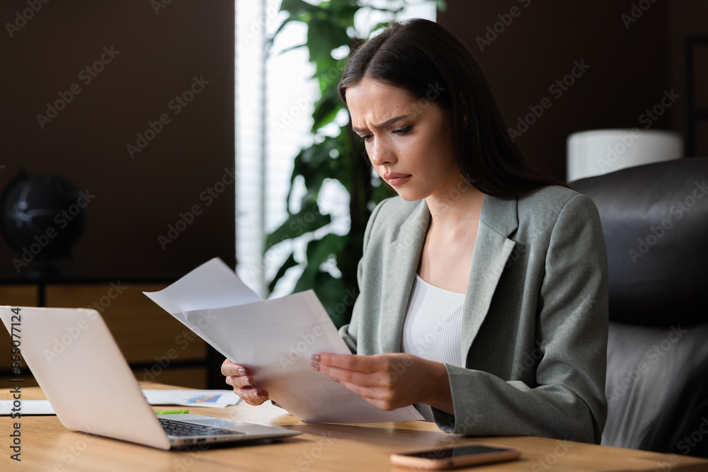 Delighted young buisness woman in elegant suit siiting at desk holding ...