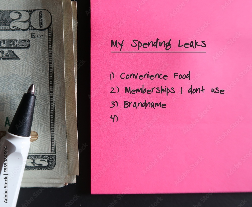 Pen, cash money, pencil, pink note with text written MY SPENDING LEAKS ...