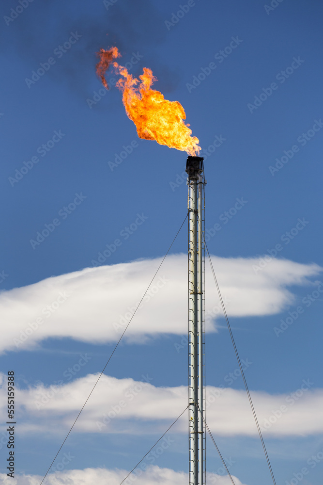 Gas plant flare with large fire flare and black smoke and blue sky and ...